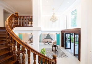 Um interior espaçoso com uma escadaria de madeira, um candelabro e vista através de grandes janelas.