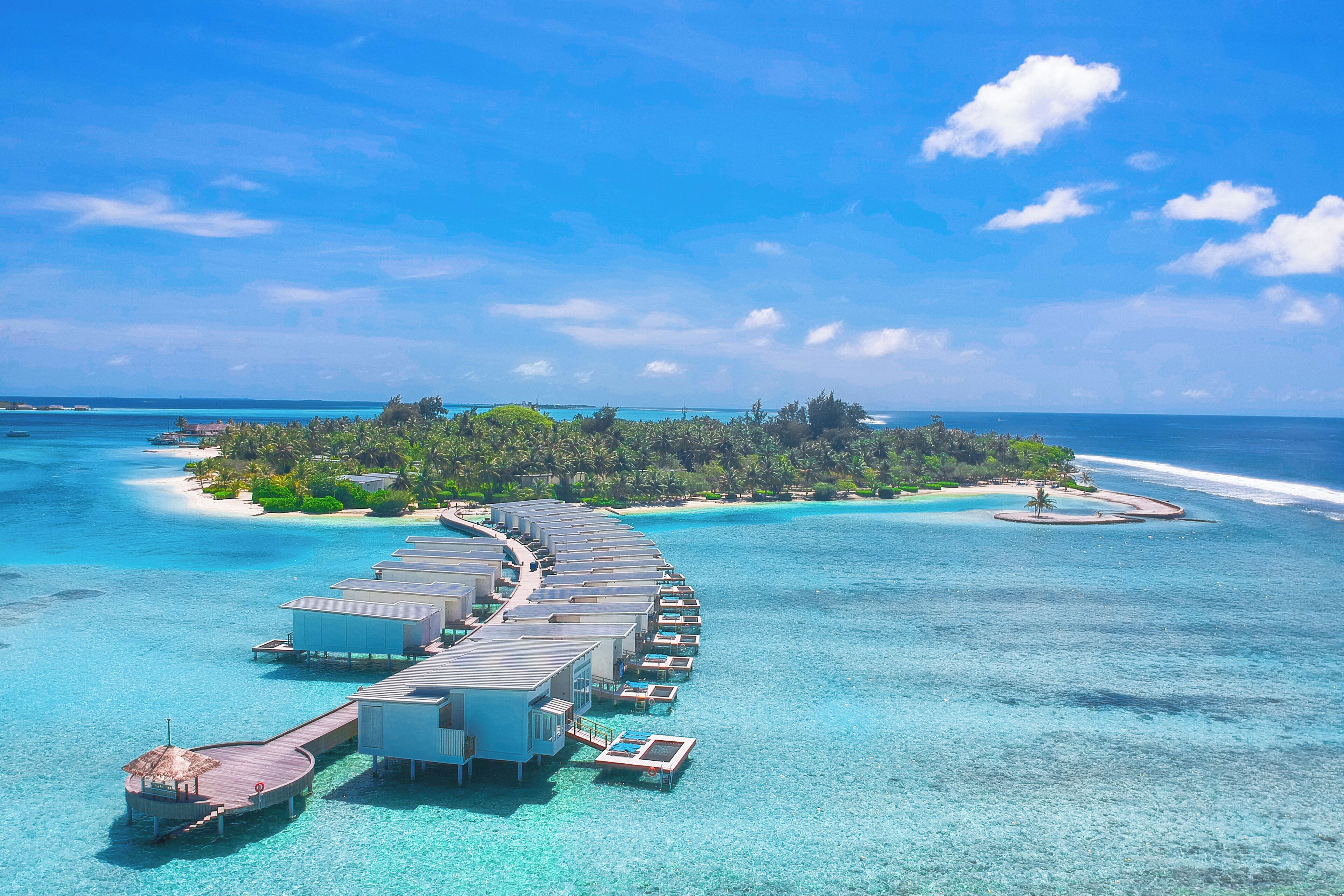 Bungalôs sobre a água com águas turquesa cristalinas e uma ilha tropical ao fundo.