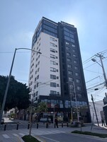 Um edifício de vários andares com uma placa grande que diz 'LIVING', apresentando um design arquitetônico moderno com uma combinação de elementos de fachada em vidro e painéis sólidos.