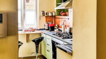 Uma cozinha com fogão a gás, luminária pendente e janela com cortinas.