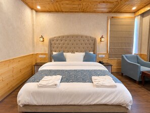 Quarto de hotel com cama grande, duas mesinhas de cabeceira, uma cadeira e uma janela.