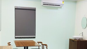 A conference room with a large screen, a ceiling fan, an air conditioning unit, a wooden table with chairs, and a marble floor.