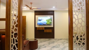 A modern living room with a flat-screen TV mounted on a wooden panel wall, a ceiling fan, and a marble floor.
