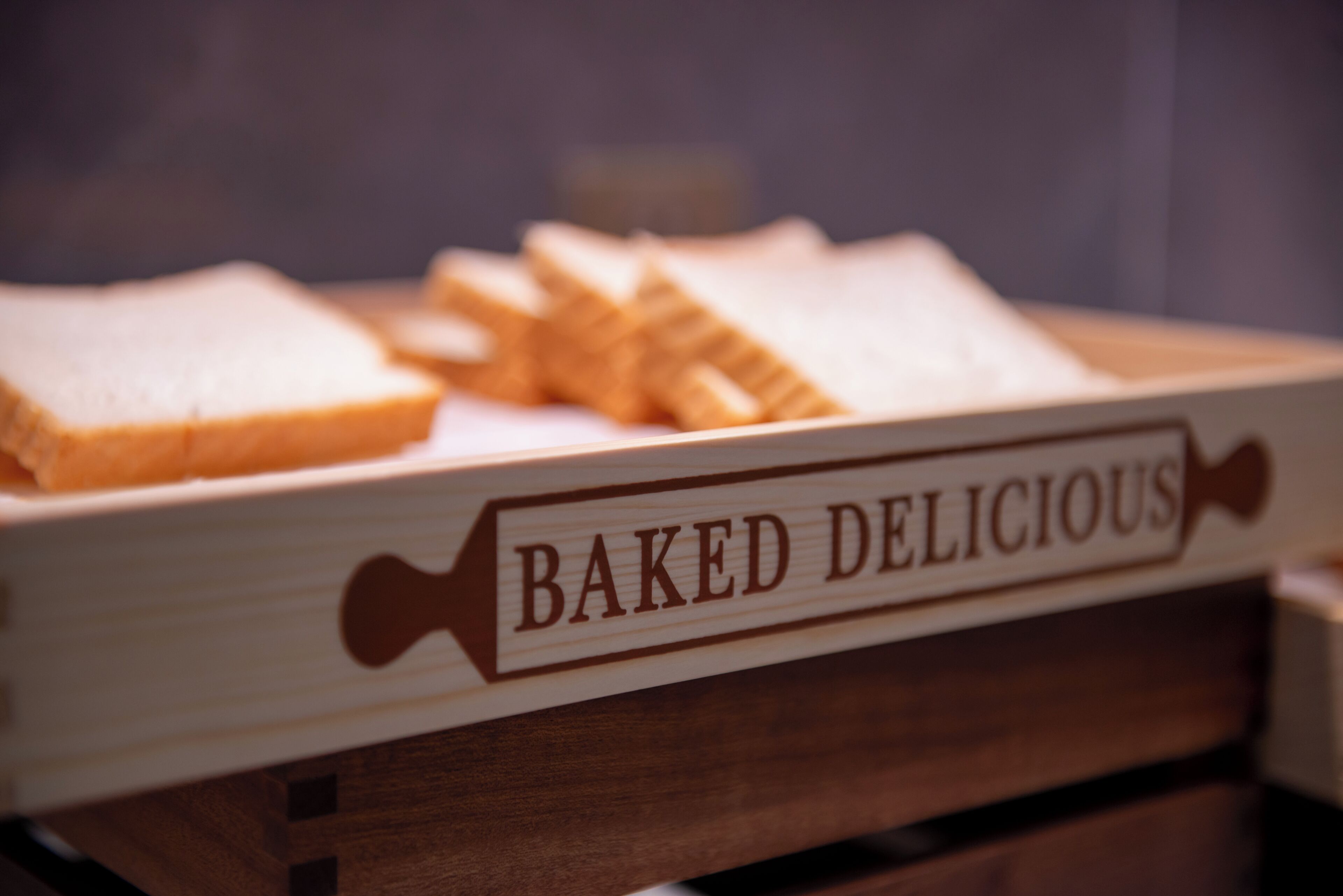 Uma caixa de madeira com a etiqueta 'BAKED DELICIOUS' e fatias de pão.