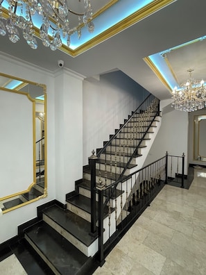 Uma escadaria imponente com corrimãos pretos e um candelabro.
