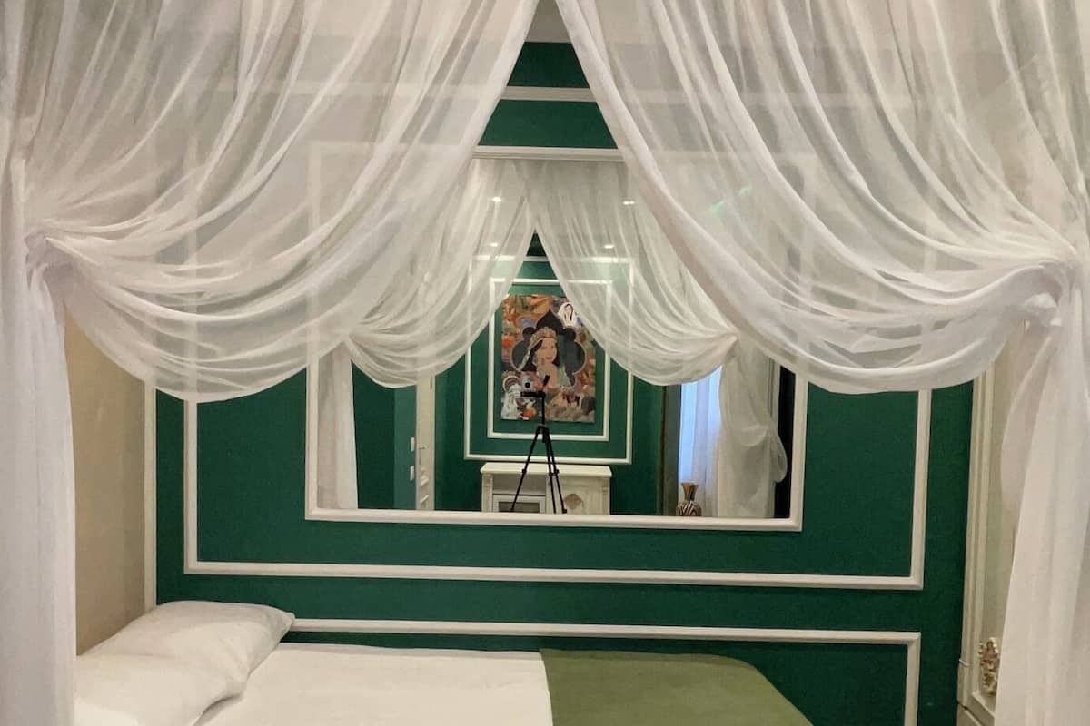 Cama com roupa de cama branca e verde, parede de destaque verde e uma pintura acima da cama.