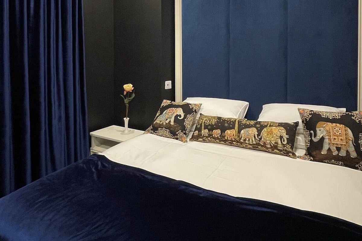 Quarto com uma cama grande, paredes escuras e janela com cortinas.