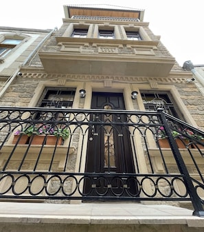 Um edifício com fachada de pedra, um portão de metal preto e caixas de flores no andar térreo.
