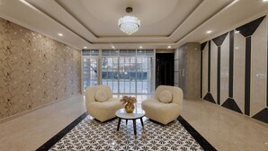 Um hall de entrada com duas poltronas, uma mesa pequena com um vaso, ladrilhos no chão com padrão e um candelabro.