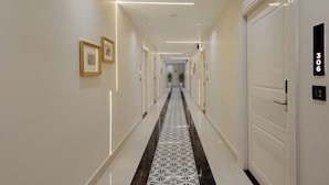 Corredor de hotel com piso estampado, obras de arte emolduradas nas paredes e portas numeradas 306.