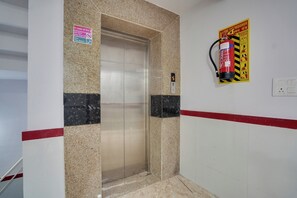 Um elevador com sinal de segurança contra incêndio, extintor de incêndio e visor digital indicando o andar.