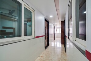 Um corredor com portas de vidro, paredes brancas e chão de mármore.