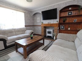 Uma sala de estar com sofá, mesa de centro, lareira e uma TV de tela plana acima.