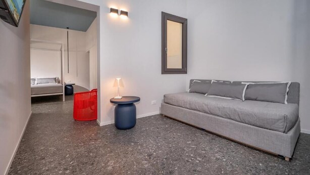 Uma sala de estar moderna com um sofá cinzento, uma cesta vermelha, uma mesinha lateral azul e um espelho fixado na parede.