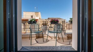 Varanda com duas cadeiras e uma mesa, com vista para um edifício com telhado de azulejos e céu claro.