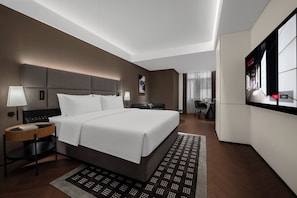 Quarto de hotel moderno com uma cama grande, mesas de cabeceira, uma escrivaninha e um espaço de estar.