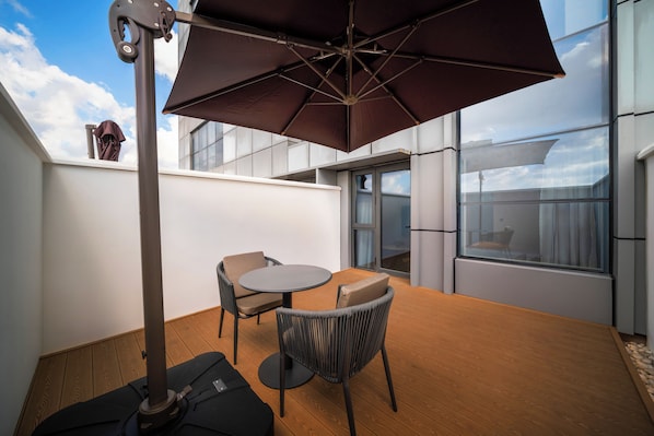Terraço no telhado com mesa e cadeiras, um grande guarda-sol e vista do céu.