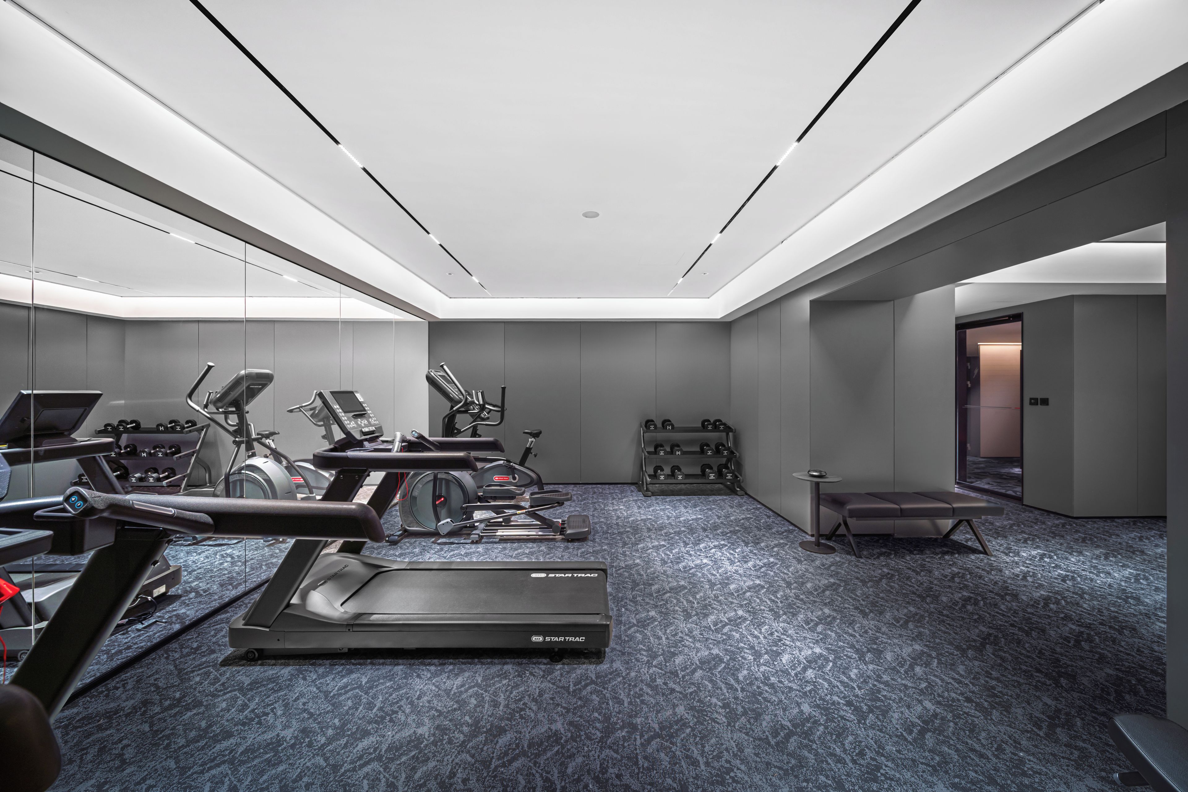 Academia moderna com diversos equipamentos de exercício, um banco e uma pequena mesa.