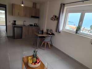 Uma cozinha moderna com armários de madeira, uma área de refeições com mesa e cadeiras, e vista para o mar através de uma grande janela.