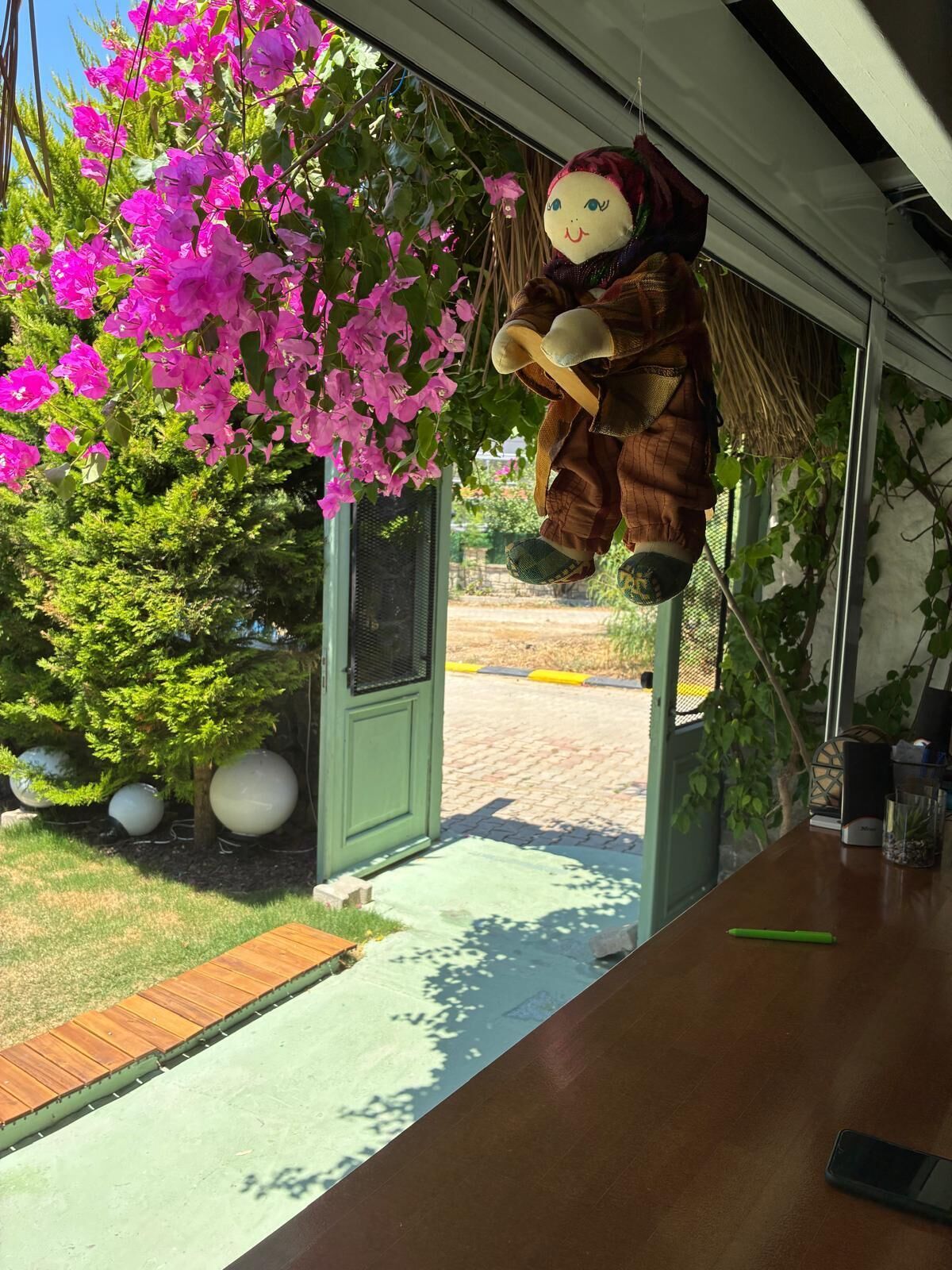 Um quarto com uma janela grande, uma boneca pendurada e uma porta verde.