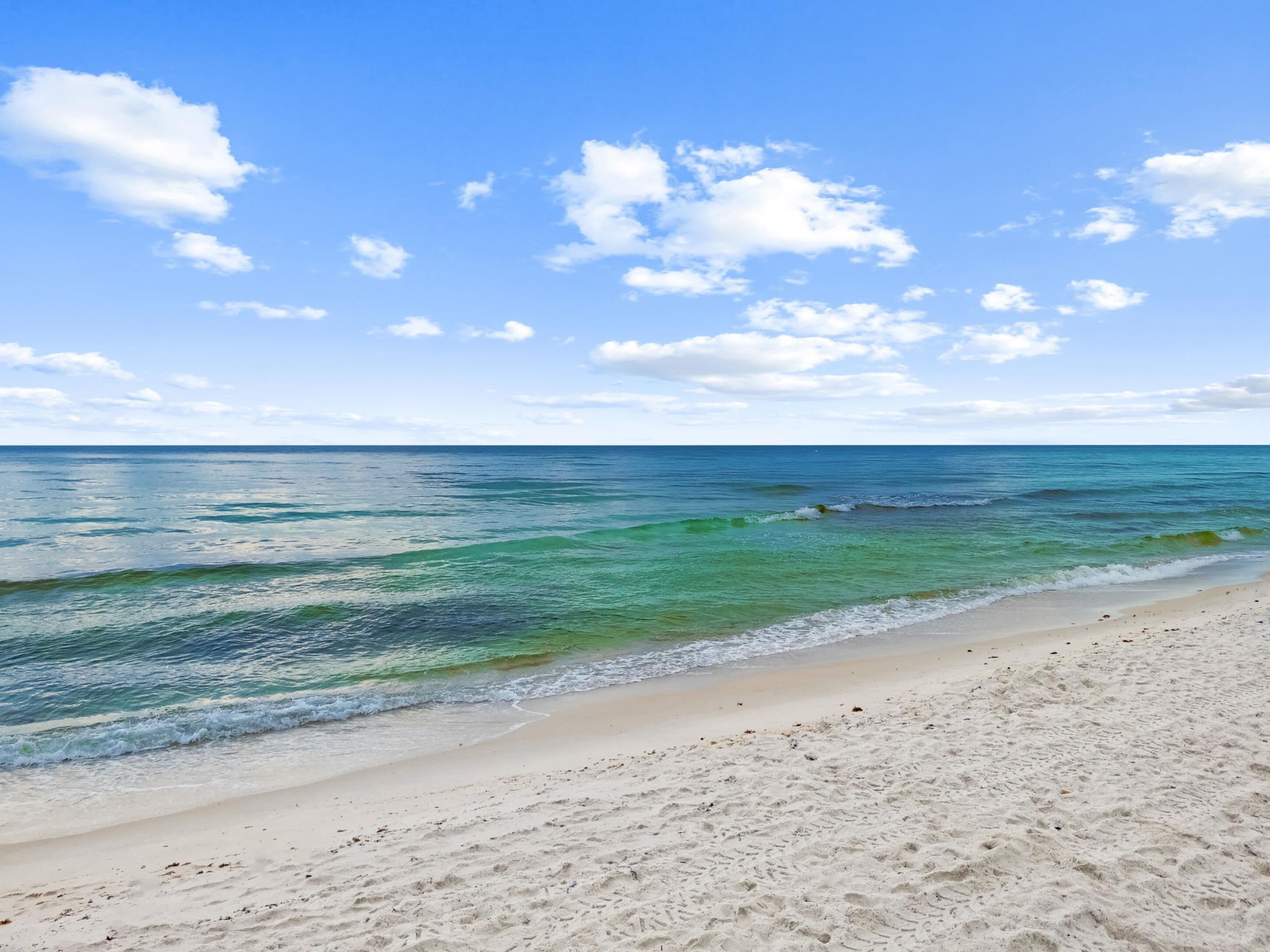 Uma praia com águas azuis cristalinas, areal arenoso e céu parcialmente nublado.