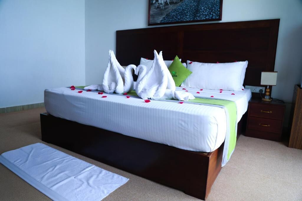 Quarto de hotel com uma cama, mesa de cabeceira, abajur e um quadro na parede.