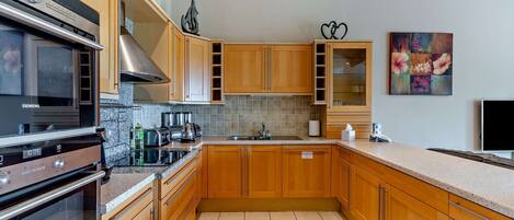 Cozinha com armários de madeira, forno de aço inoxidável, micro-ondas e painel de azulejos.