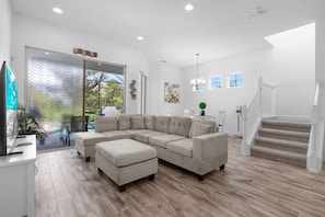 Uma sala de estar moderna com um sofá modular, uma porta de vidro que dá para uma varanda e uma escada.