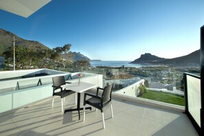 Terraço com mesa e cadeiras, com vista para a paisagem costeira, montanhas e o mar.
