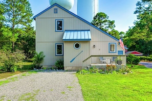 Uma casa de dois andares com varanda, uma bandeira e um silo ao fundo.