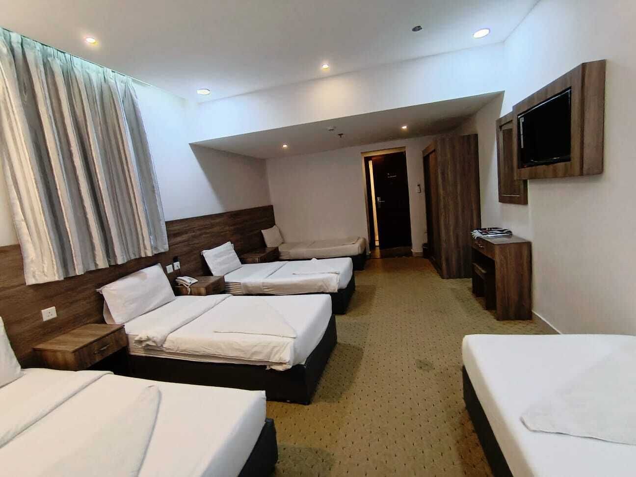Quarto de hotel com quatro camas de solteiro, televisão fixada na parede e cabeceira de madeira.