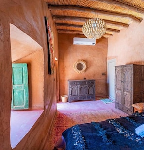 Quarto rústico com teto de madeira, cama com colcha estampada, cômoda e porta verde.