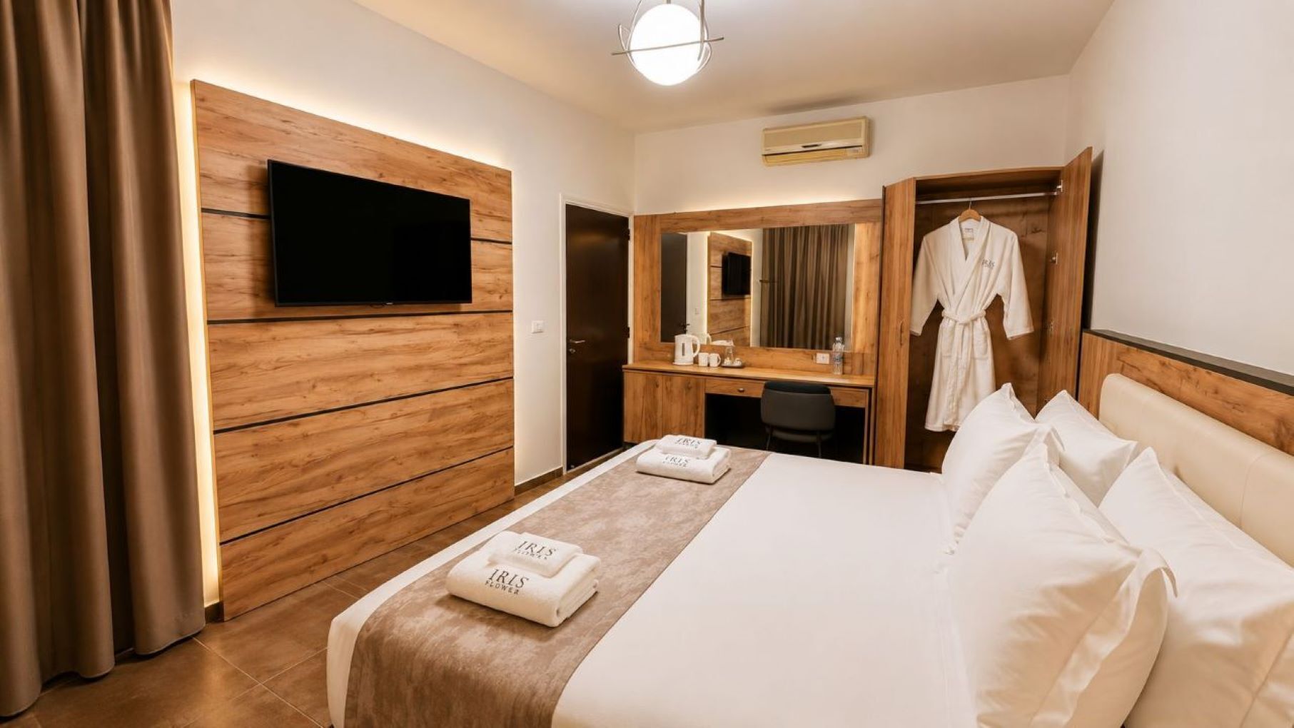 Quarto de hotel com cama, escrivaninha, espelho, roupão e televisão.