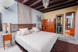 Quarto com uma cama grande, cabeceira de madeira, duas mesas de cabeceira, um guarda-roupa e uma cadeira.