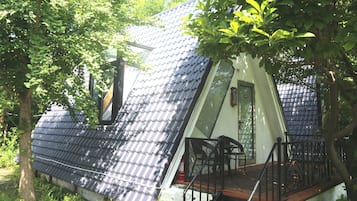 Um pequeno edifício térreo com telhado inclinado, escadas que levam a um alpendre e uma porta com uma placa.