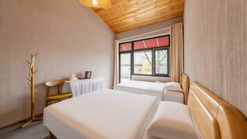 Quarto de hotel com duas camas, teto de madeira, janela com cortinas vermelhas e uma mesa com abajur.