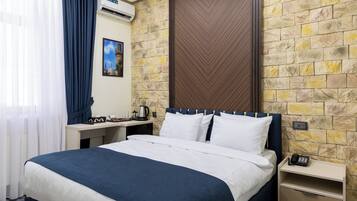Quarto de hotel com cama, mesa de cabeceira, cafeteira, controle remoto e um quadro na parede.