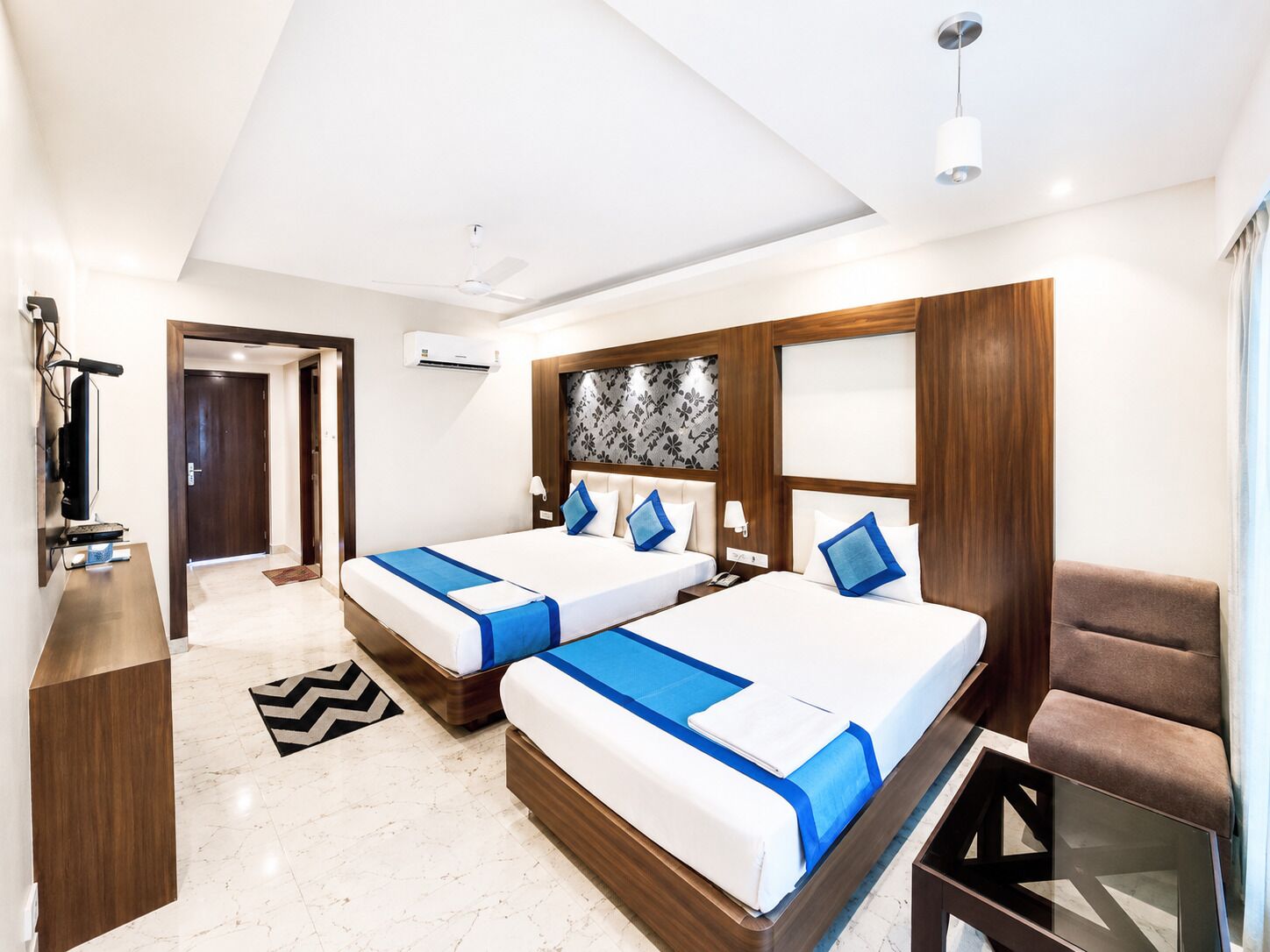 Quarto de hotel com duas camas, uma escrivaninha, uma cadeira, uma televisão e ar condicionado.