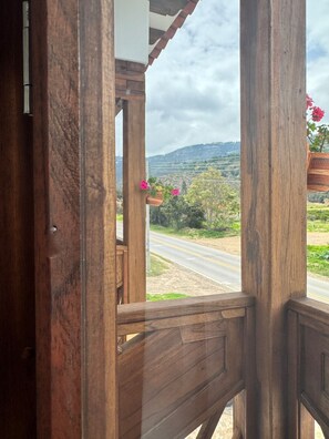 Uma varanda de madeira com vista para uma estrada e colinas ao longe.