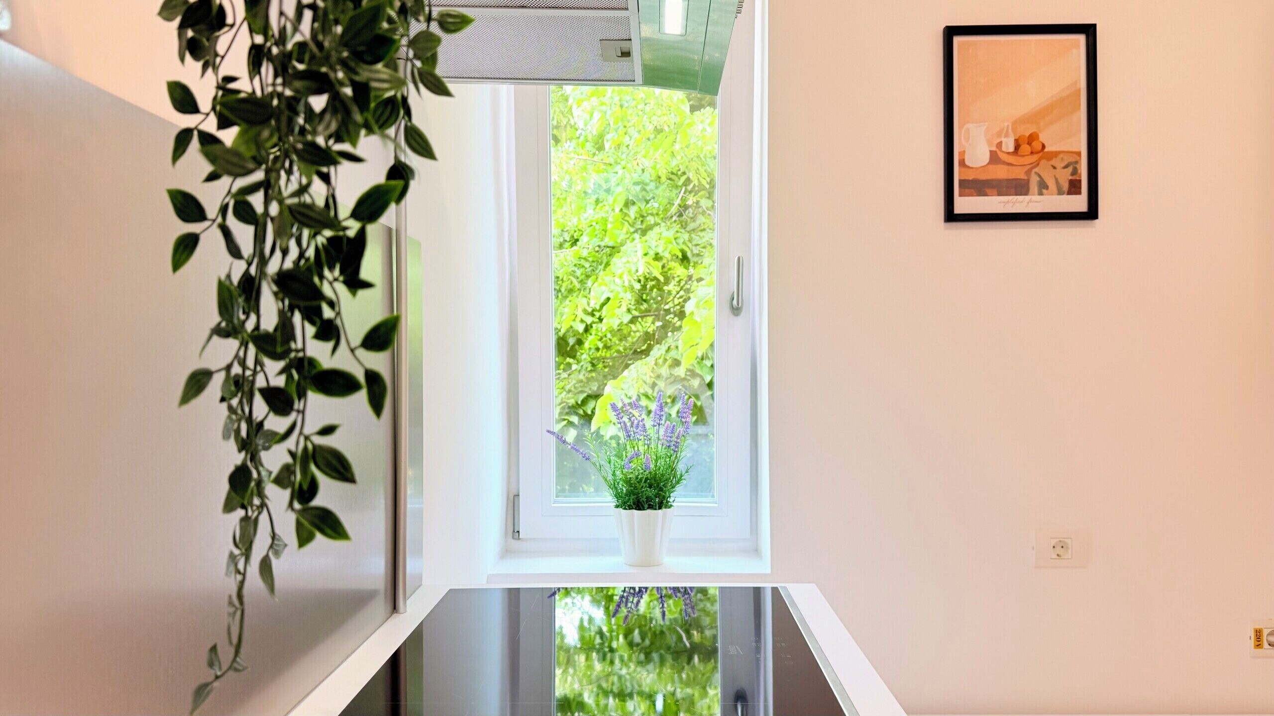 Um quarto com janela, uma planta e um quadro na parede.