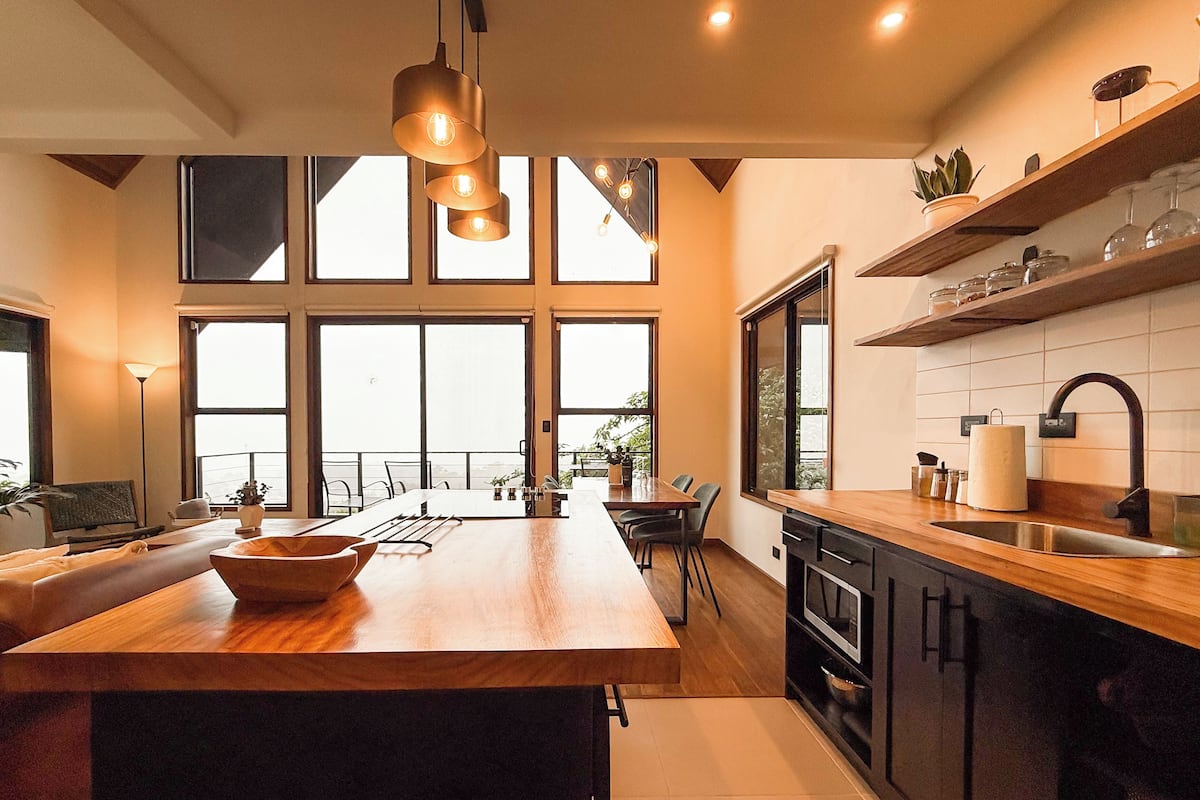 Cozinha moderna com ilha central, janelas amplas e área de jantar com vista.