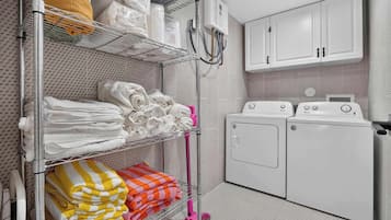 Uma lavanderia com máquina de lavar, secadora, prateleiras de metal com toalhas dobradas e um aquecedor de água.