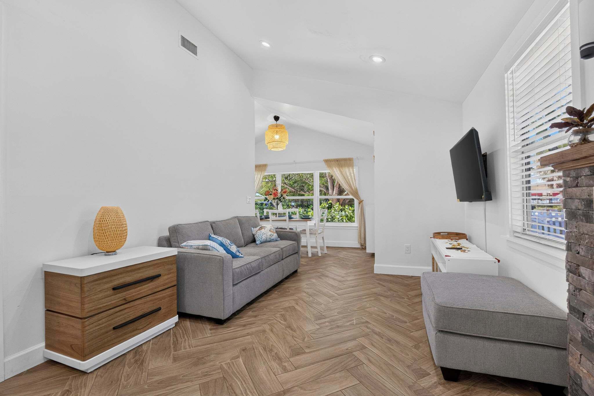 Uma sala de estar moderna com um sofá cinzento, gavetas de madeira e piso em padrão herringbone.