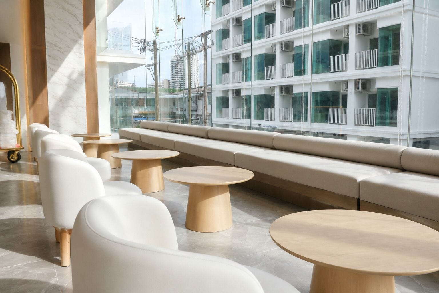Espaço lounge moderno com assentos, mesas, janelas amplas e vista para a paisagem urbana.
