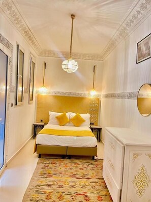 Quarto de hotel com cama, mesas de cabeceira, um candelabro e um tapete estampado.