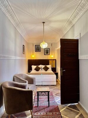 Quarto de hotel com uma cama, uma cadeira, uma mesa pequena e um tapete estampado.