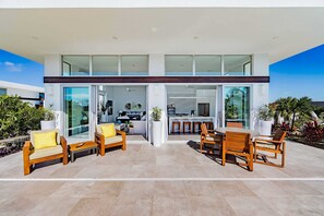 Uma casa moderna com área de varanda, móveis de exterior e cozinha visível através de portas de vidro.