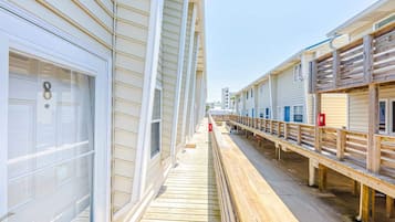 Um calçadão de madeira que leva a uma fileira de cabanas à beira-mar, com grandes janelas e céu claro.