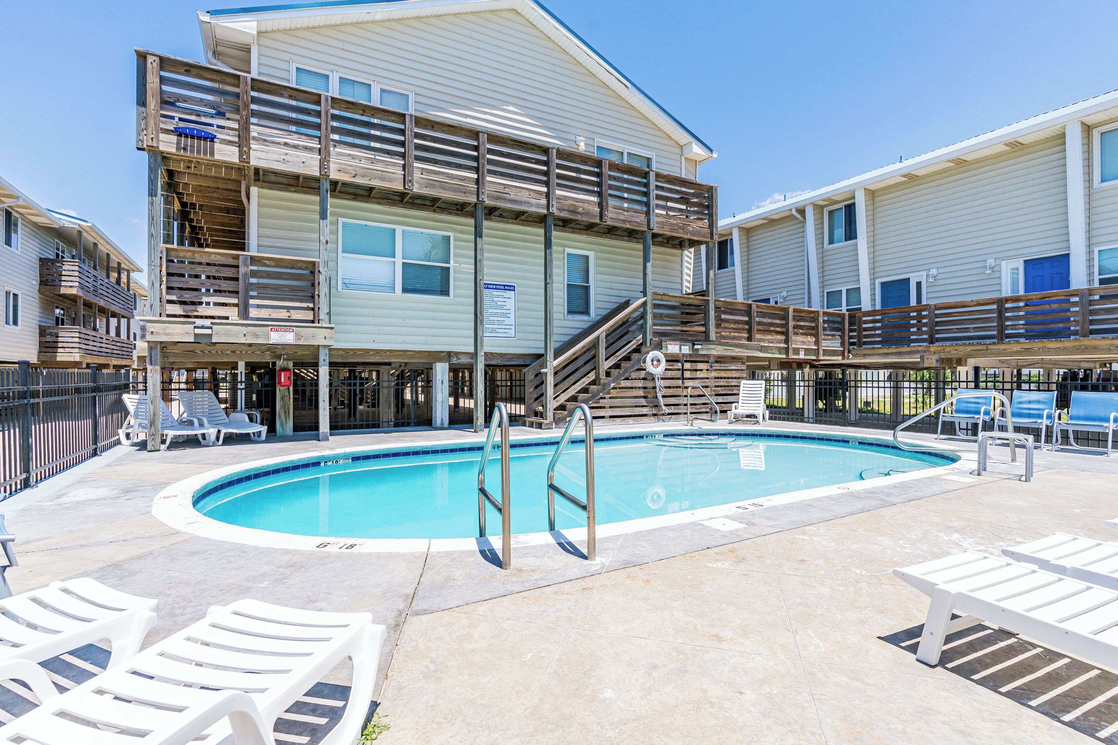 Área da piscina com deck de madeira, espreguiçadeiras e um aviso com as regras da piscina.
