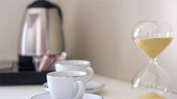 Uma xícara de café branca, uma ampulheta de vidro e uma cafeteira de prata sobre uma mesa.